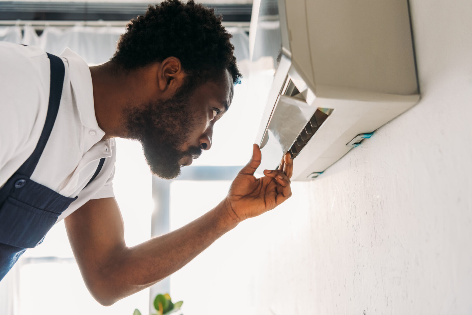 concentrated african american repairman looking at broken air ...